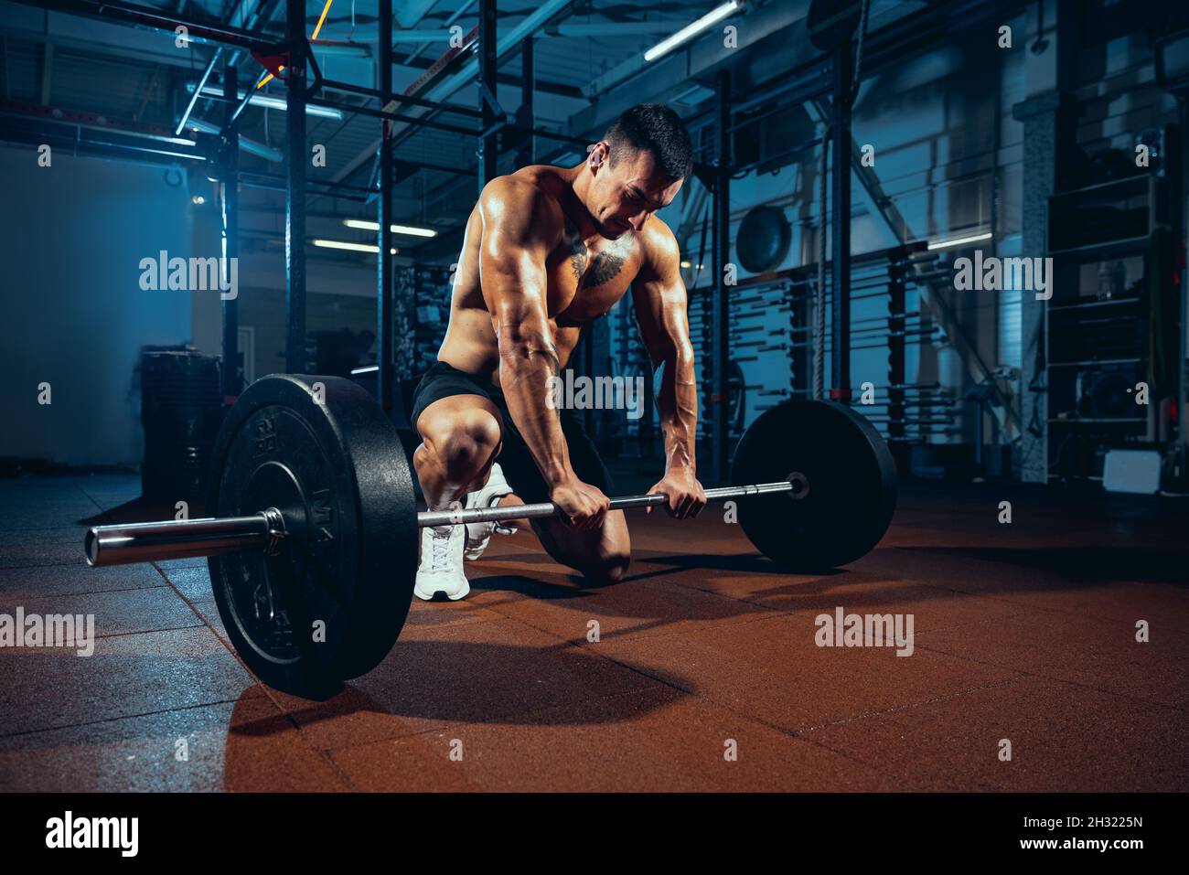 Young strong man, muscled athlete, bodybuilder training alone at sport ...