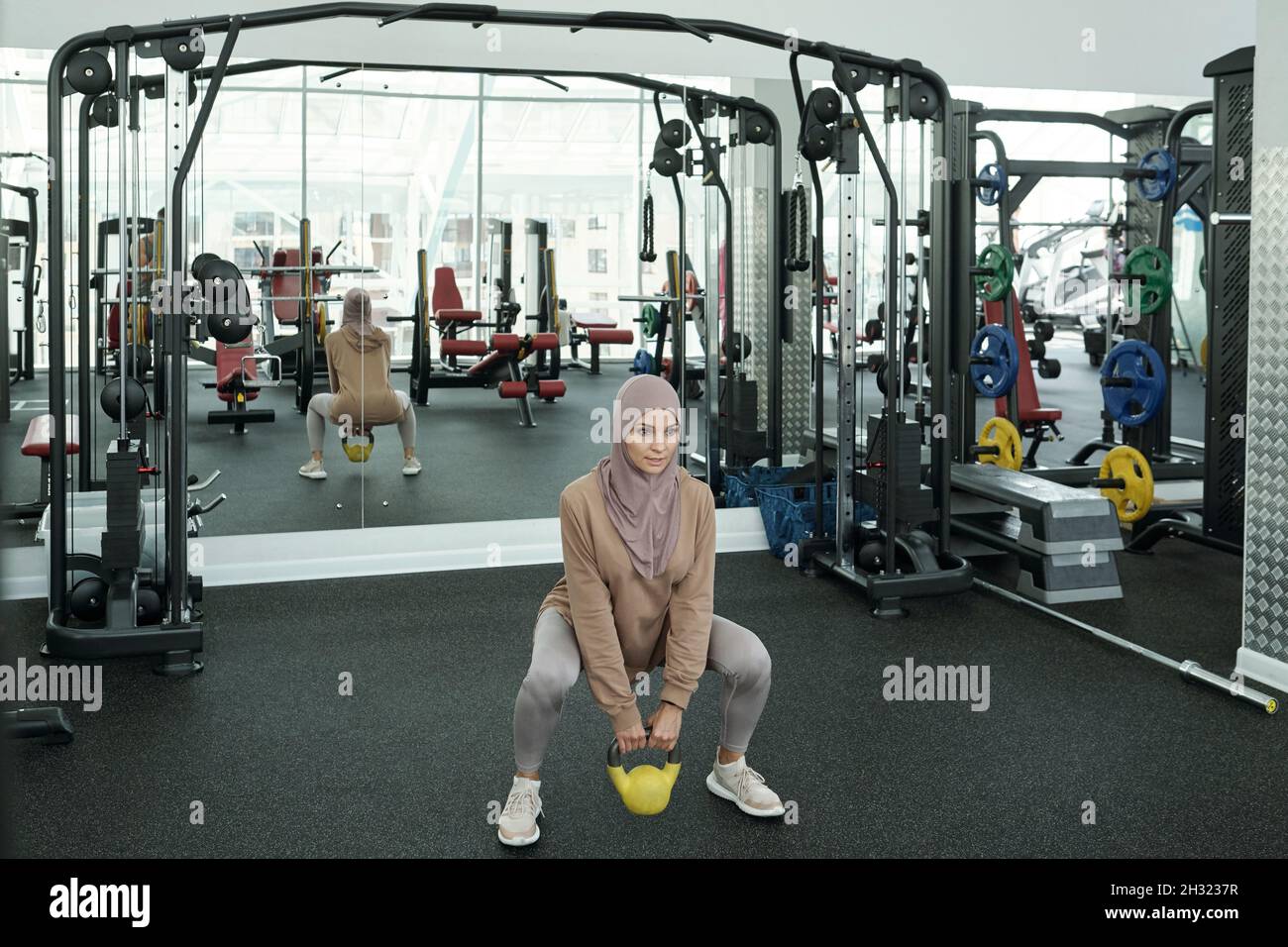 Young strong Muslim woman with heavy weight exercising on knee bent ...