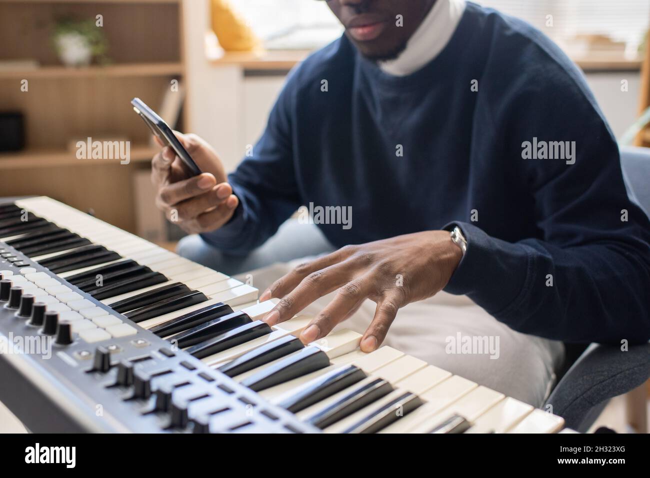 Young male teacher of music with smartphone touching keys of piano ...