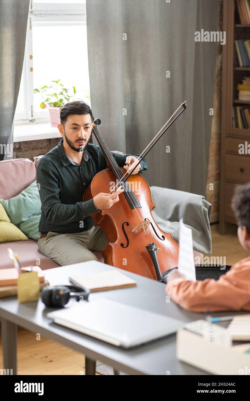 Young confident music teacher explaining schoolboy how to play cello ...