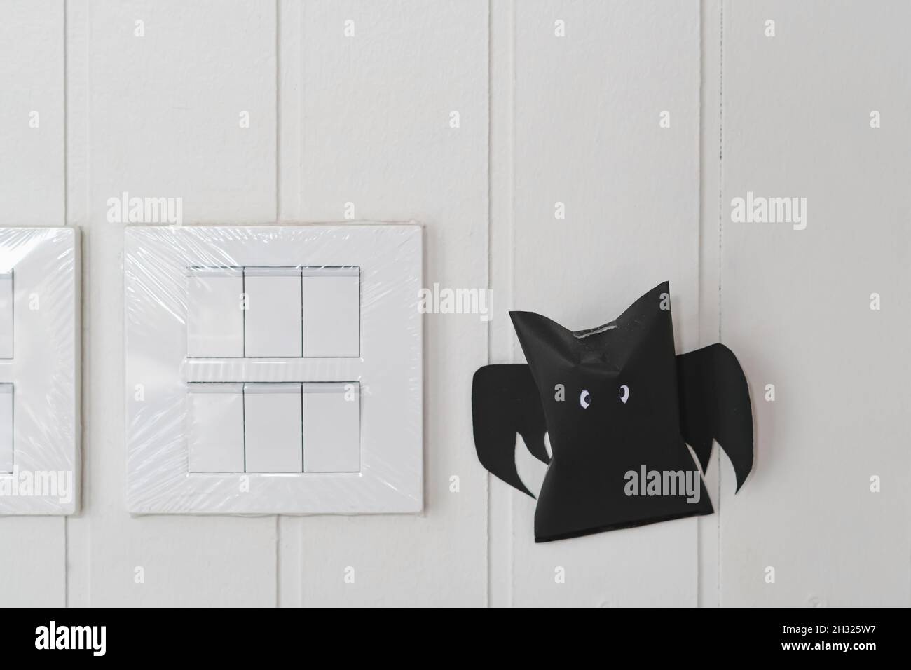 Origami bat made of black paper near light switches on white wall ...