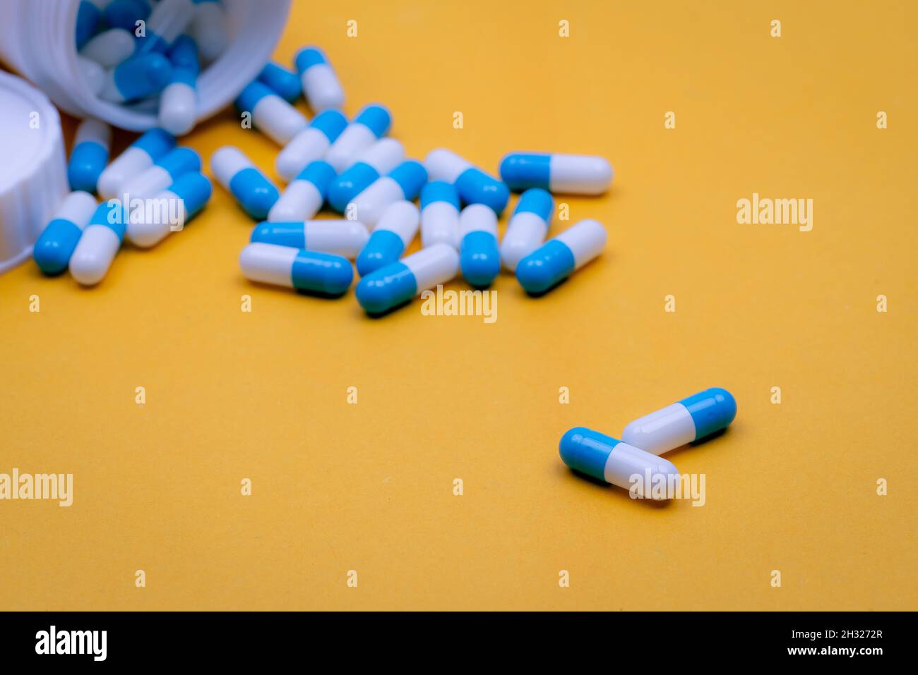 Two blue-white capsules pills on blur many of pills pouring from ...