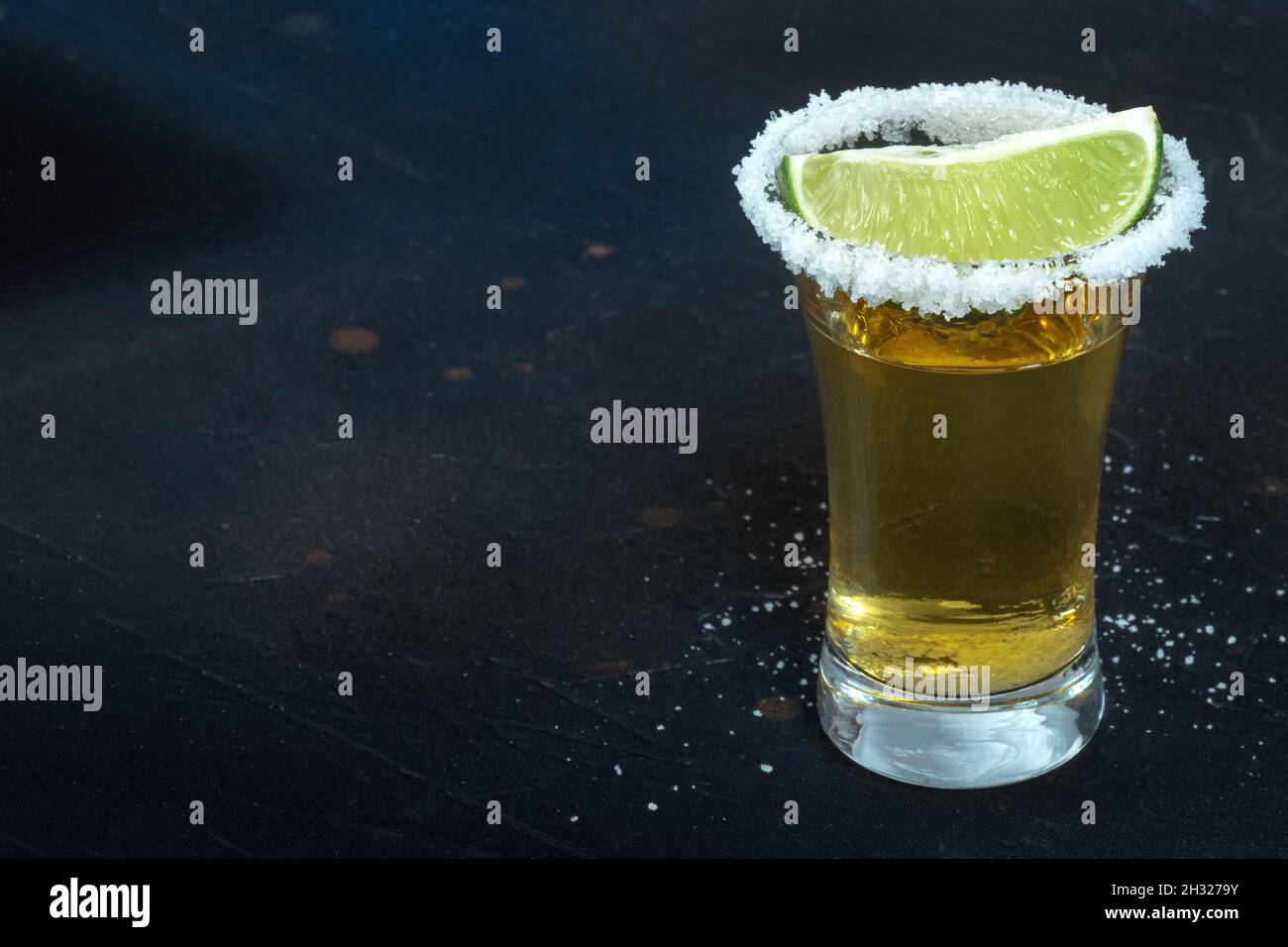 Golden tequila shot, with a salted rim and a lime slice, on a black ...