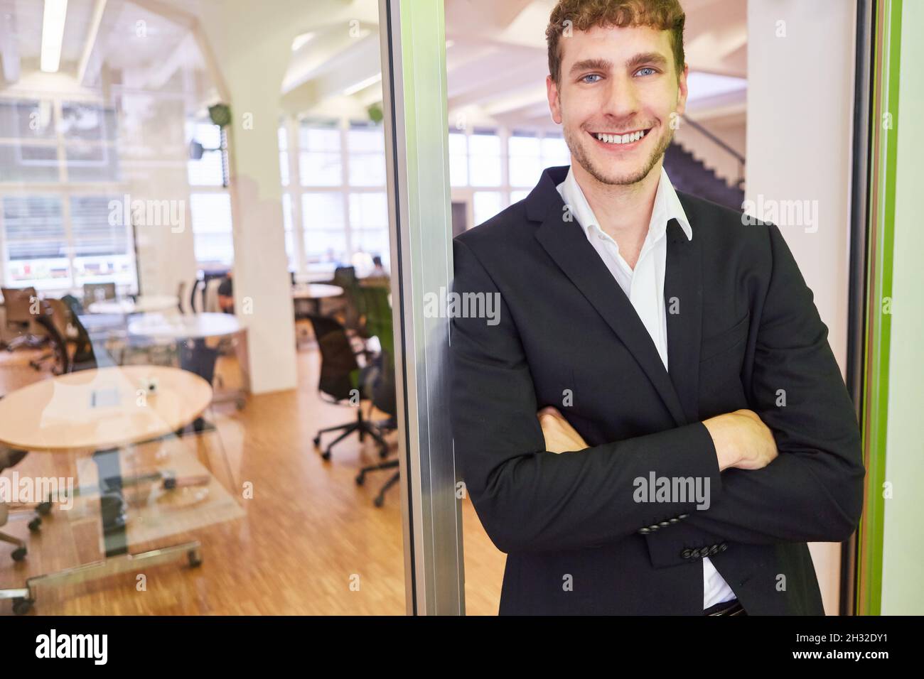 Smiling young man as a start-up founder stands in the office with his ...