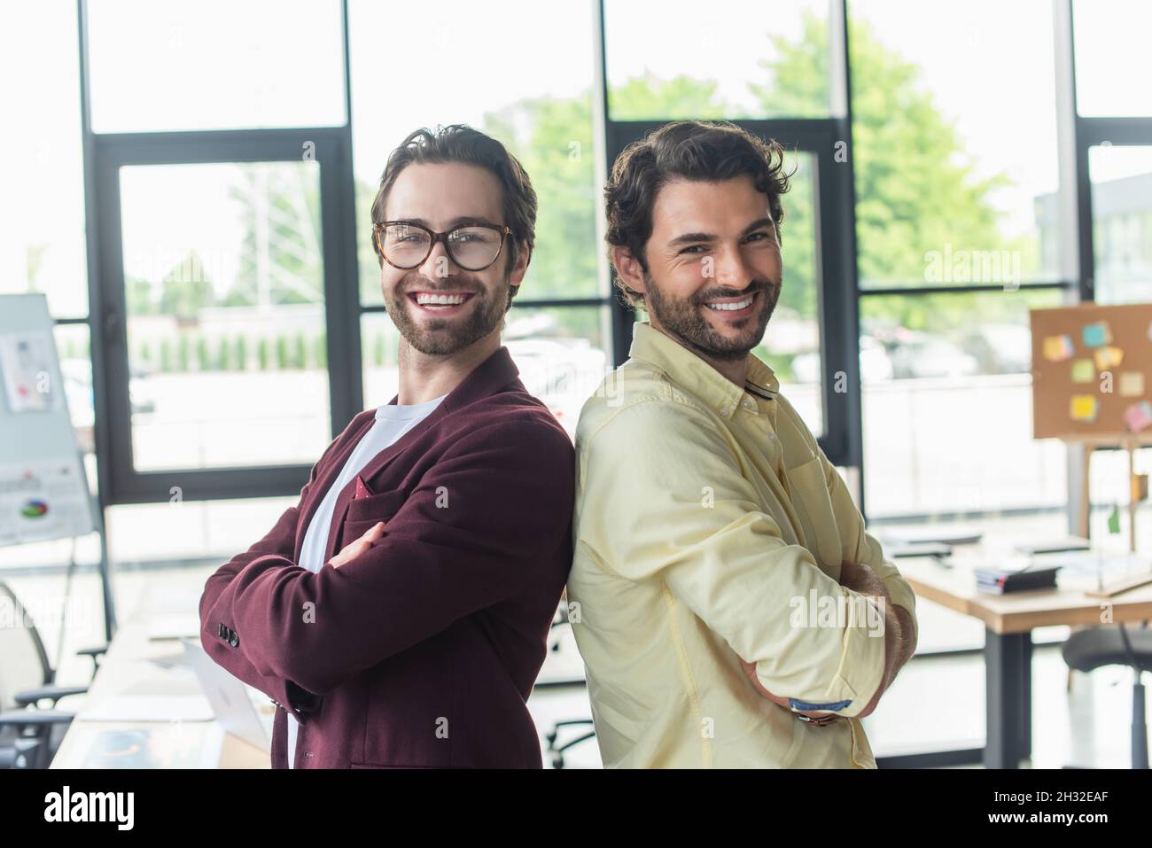 Happy businessmen with crossed arms standing back to back in office ...