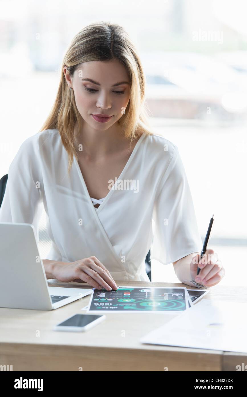 Young businesswoman holding pen near papers and gadgets in office Stock ...