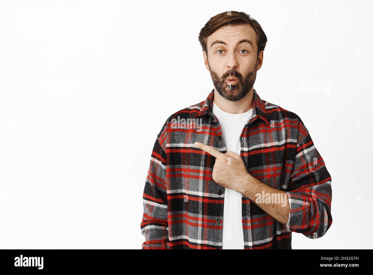 Surprised caucasian male model pointing finger left, raising eyebrows ...