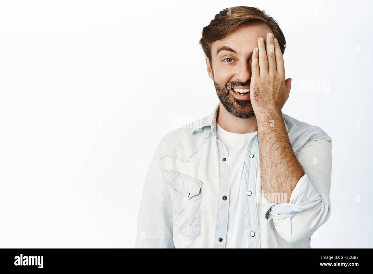 Portrait of happy guy cover half of face and smiling, looking with one ...