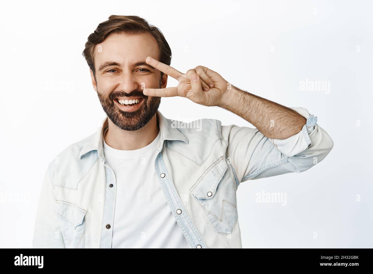 Positive smiling guy shows peace salute sign, looking happy at camera ...