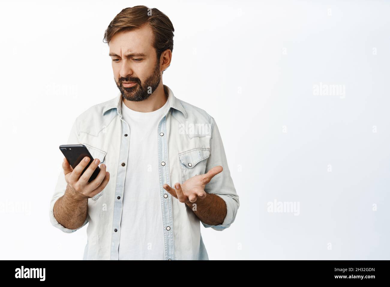 Guy looking confused at his smartphone and frowning puzzled, cant ...