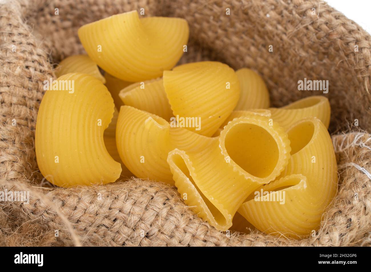 Bright yellow uncooked pasta in a jute bag, close-up, isolated on white ...