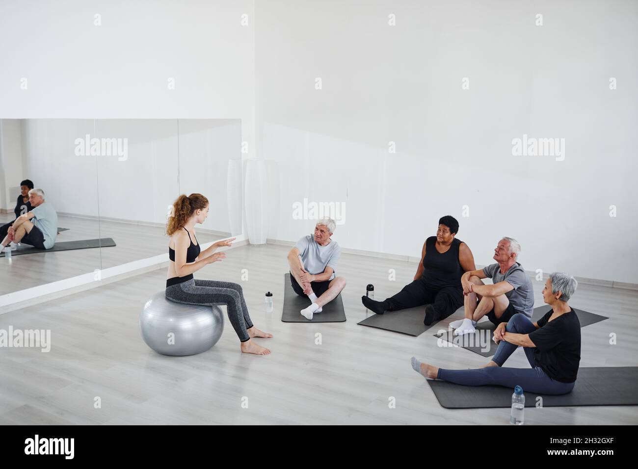Young instructor sitting on fitness ball and giving recommendations to ...
