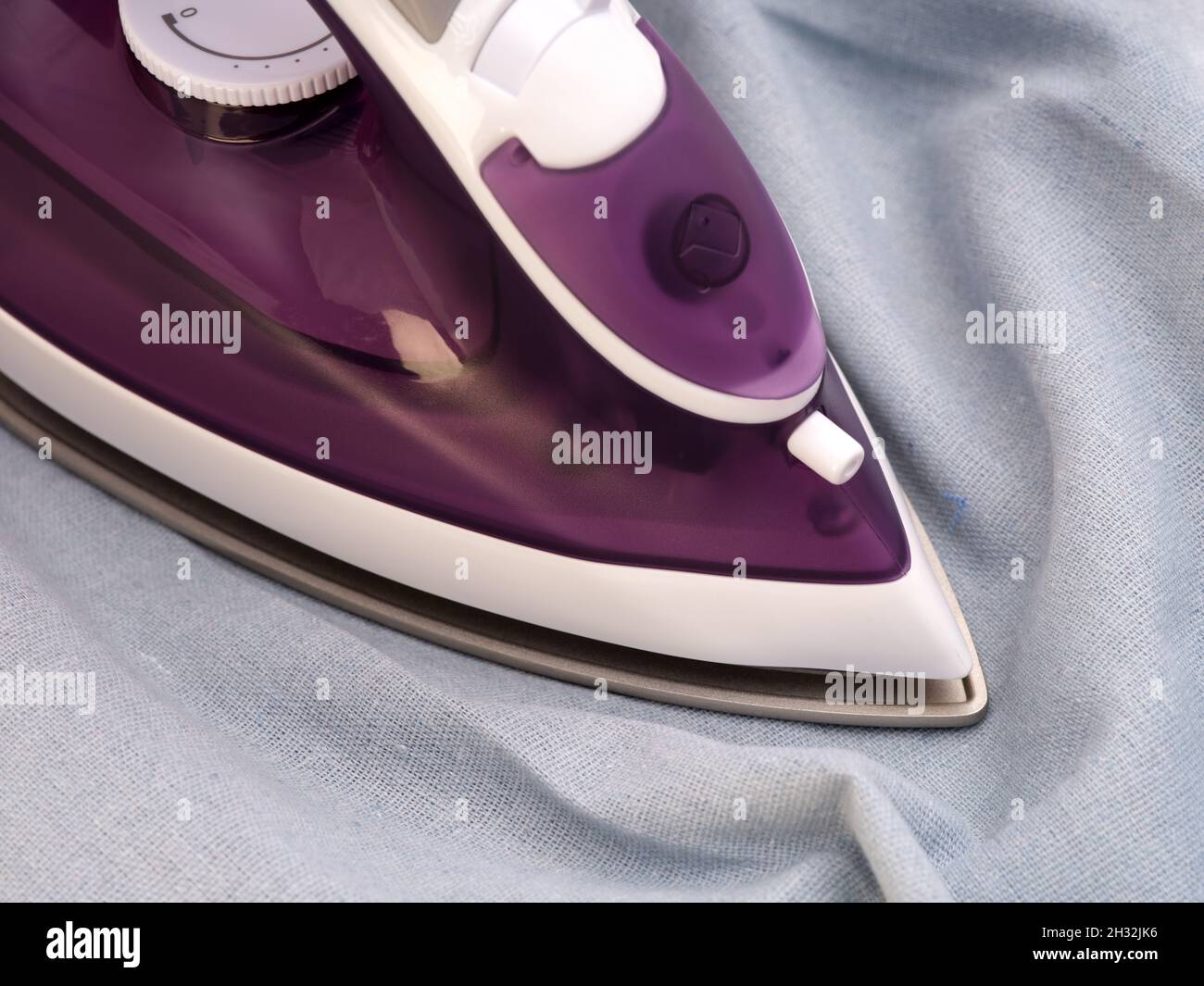 A violet iron ironing blue linen textile. Close-up Stock Photo - Alamy