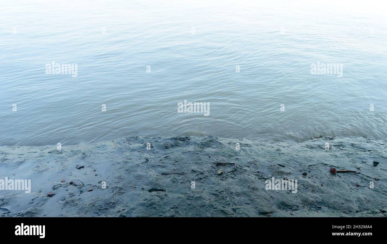 Muddy river banks in low tide next to wave water. Alluvial soils ...