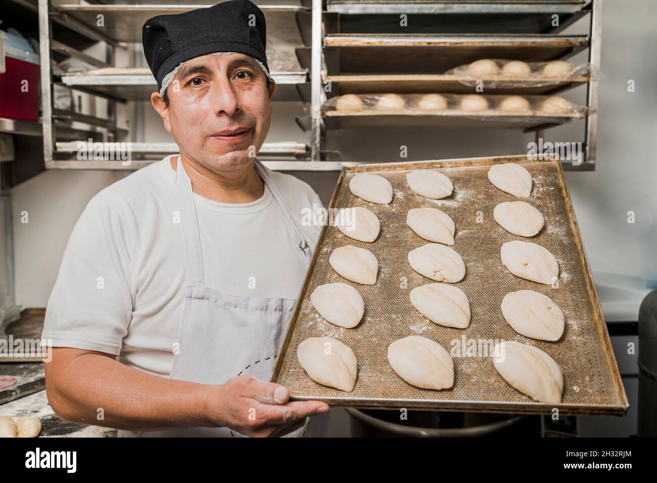 Baker with uniform showing a plate with pieces of uncooked bread ready ...