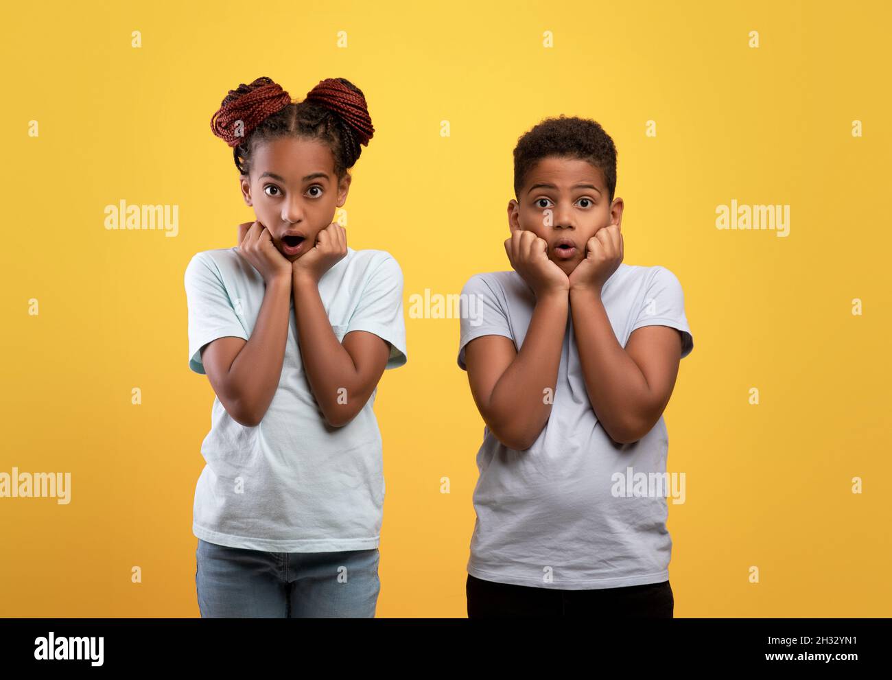 Shocked black brother and sister schoolers looking at camera, touching ...