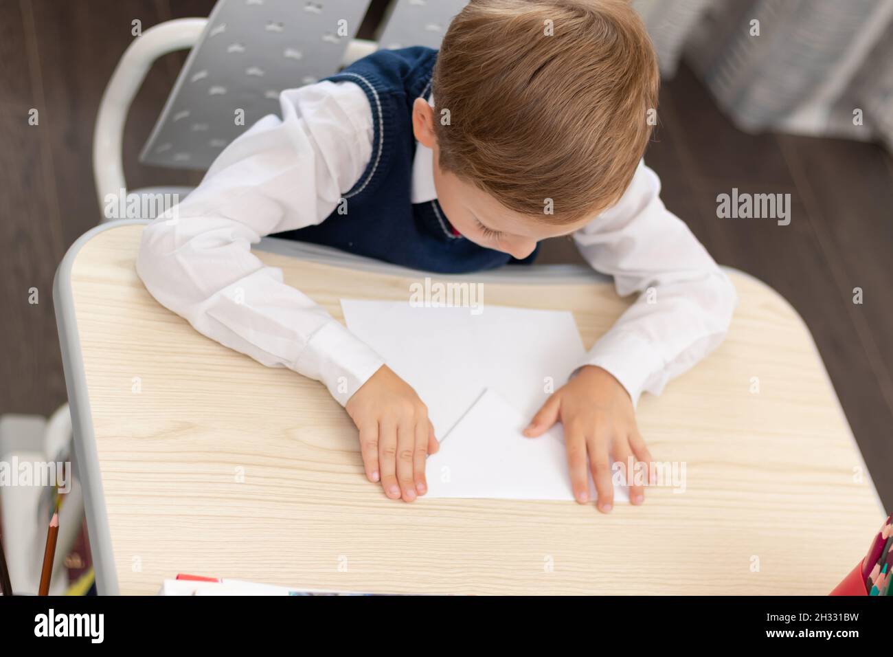 A cute first-grader boy in a school uniform at home while isolated at ...
