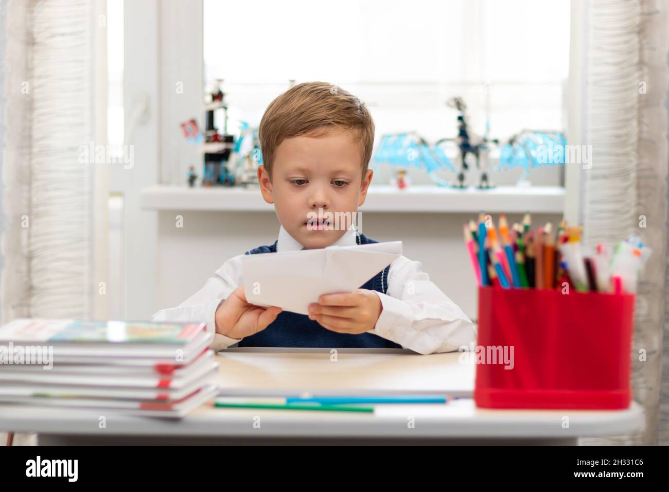 A cute first-grader boy in a school uniform at home while isolated at ...