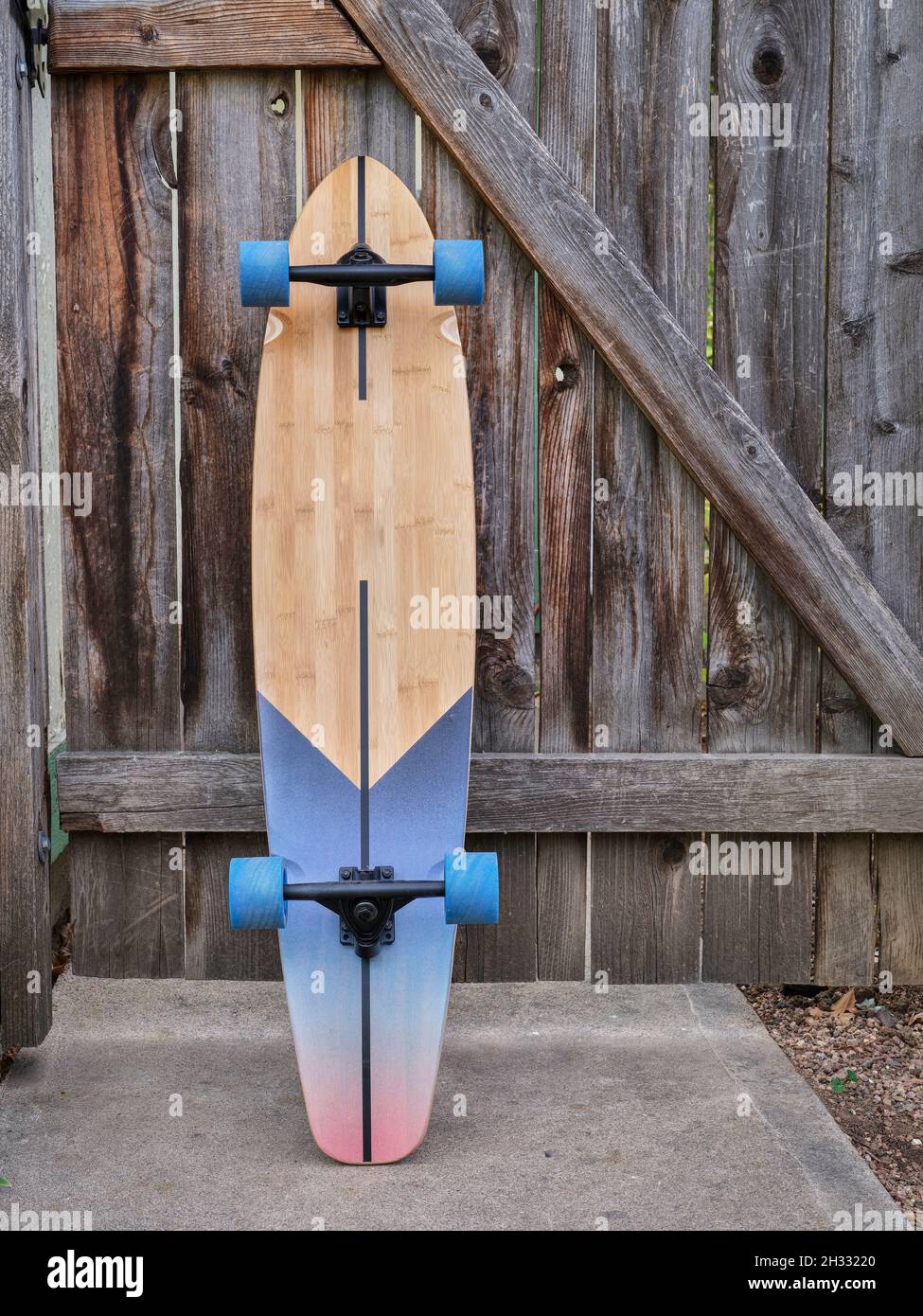 cruising longboard against a rustic wooden gate in a backyard ...