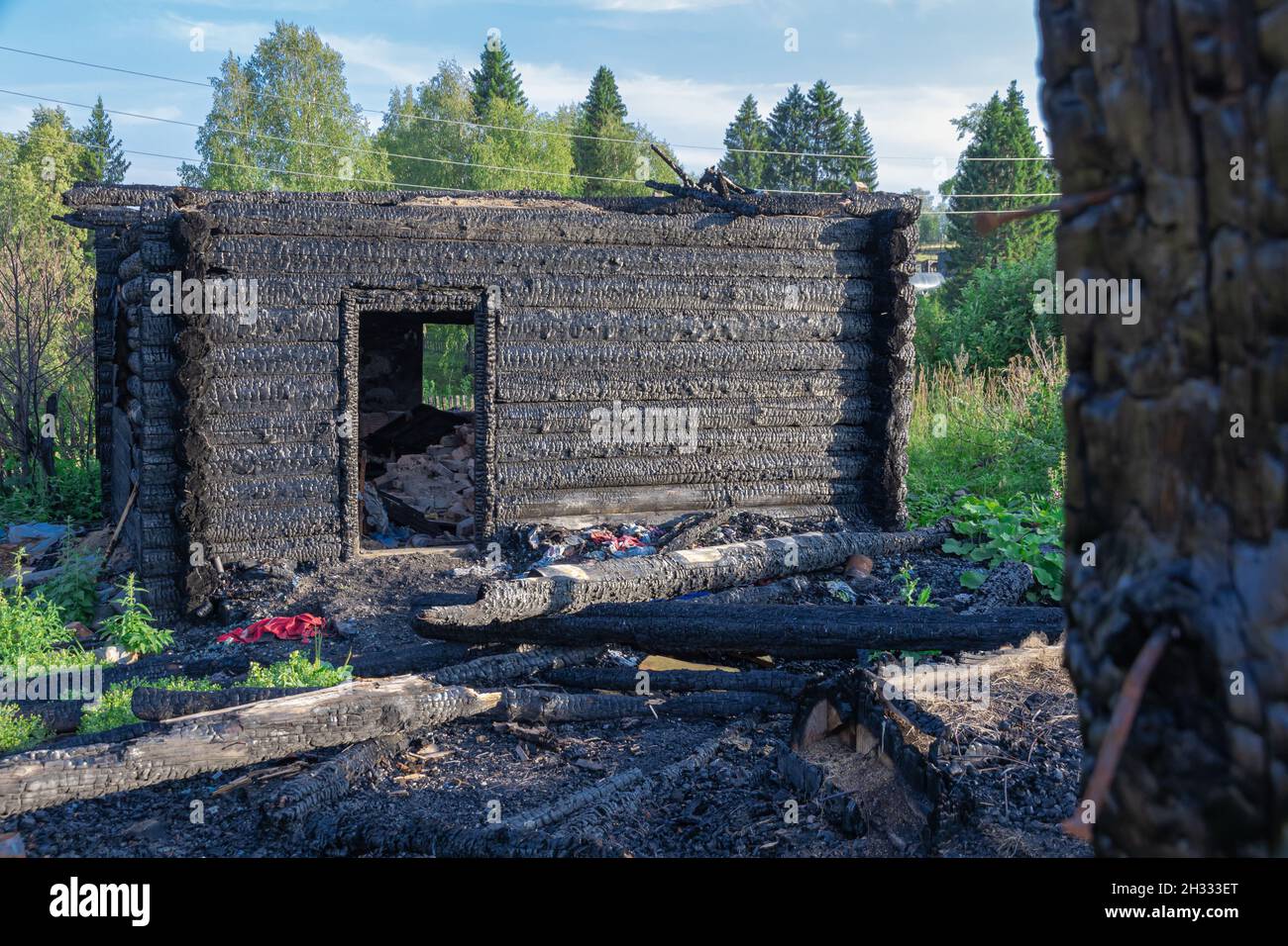 Burnt old log house in the village on a bright summer day against the ...