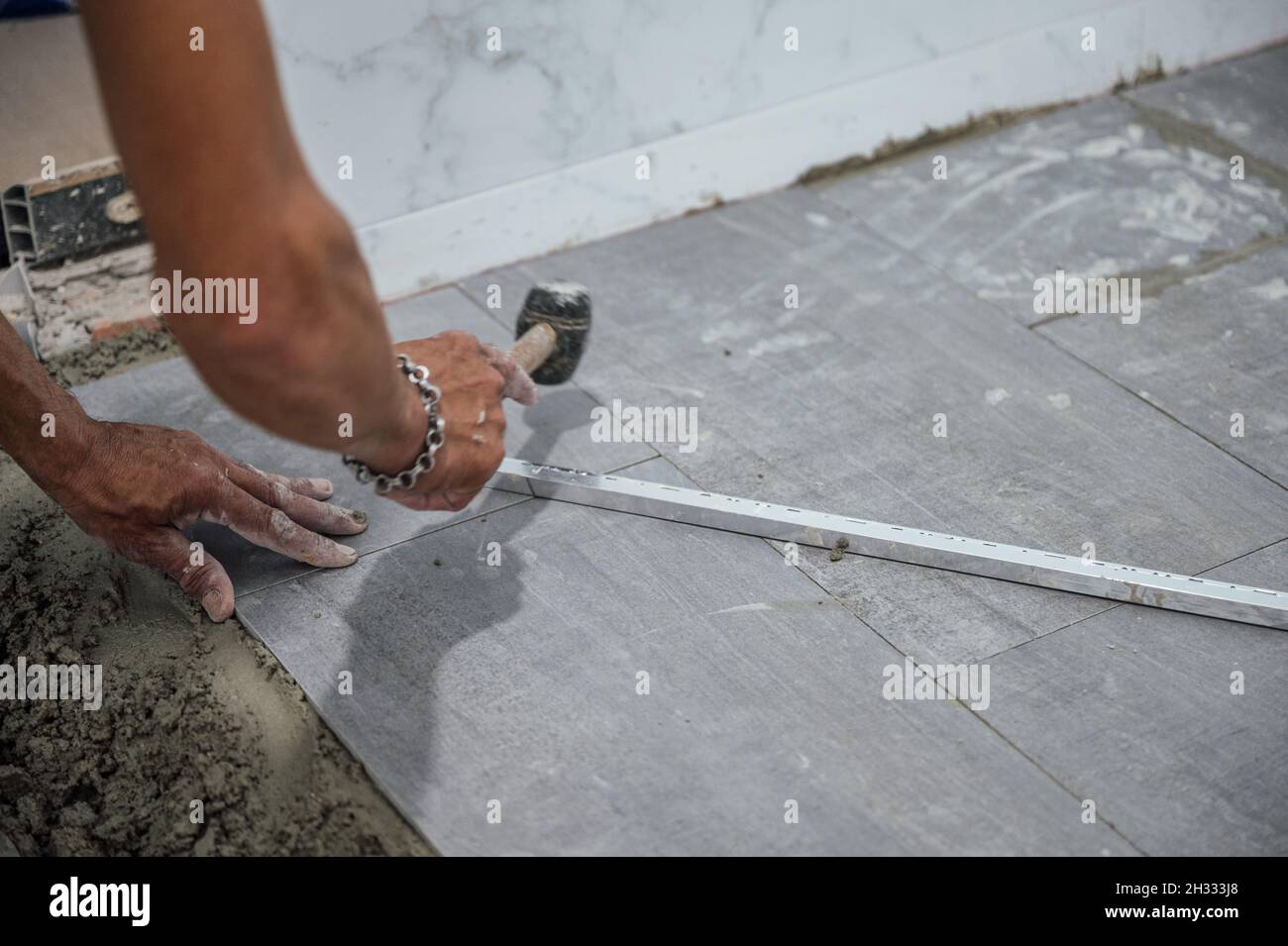 Hand of tiler laying and use mallet knocking granite tile on the floor ...