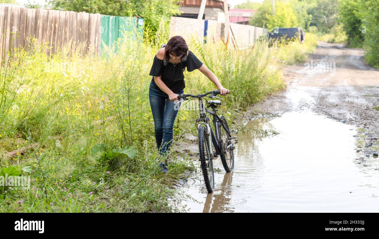 woman with difficulty drags a bicycle through the mud afraid to drive ...