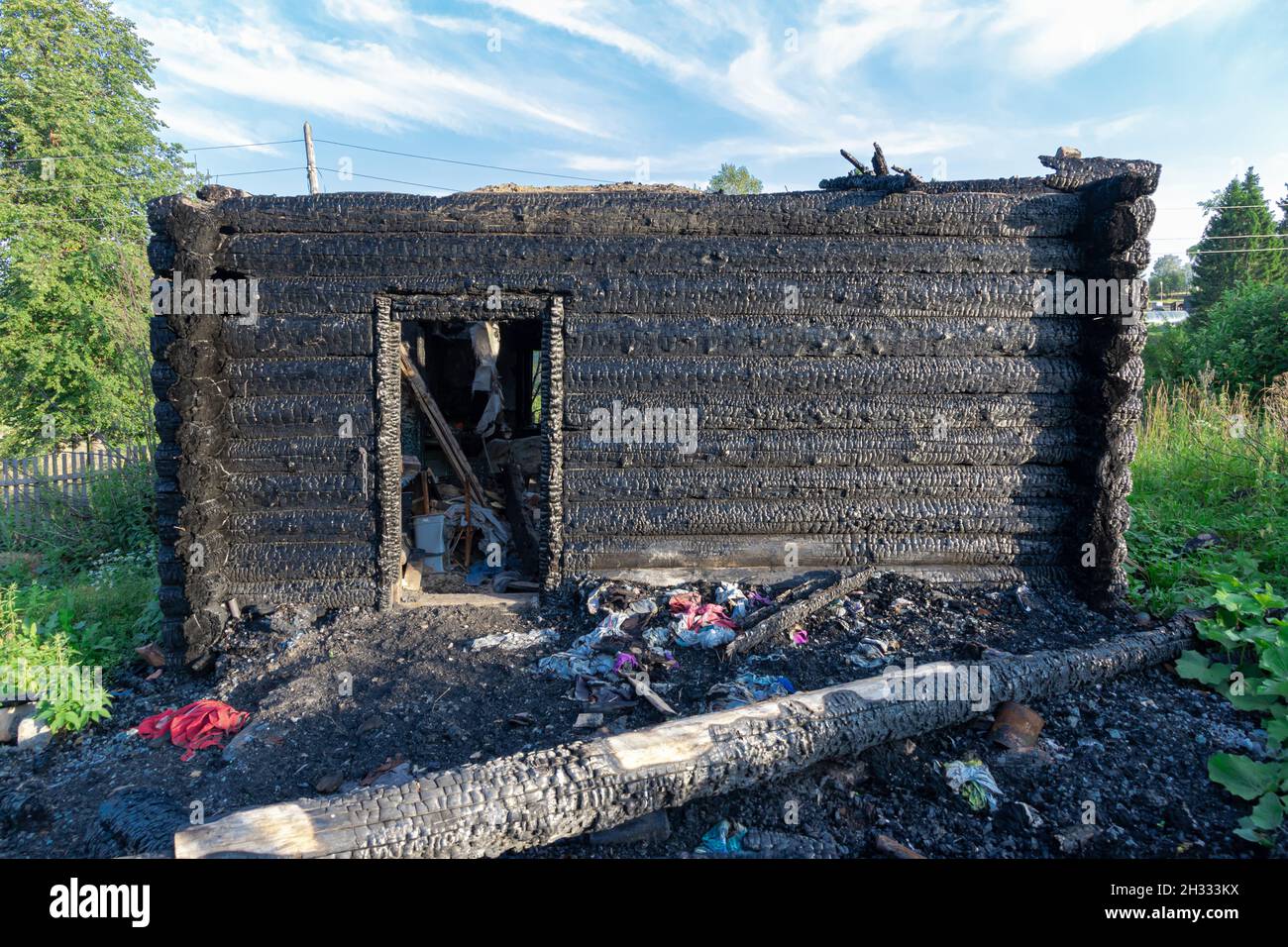Burnt old log house in the village on a bright summer day against the ...