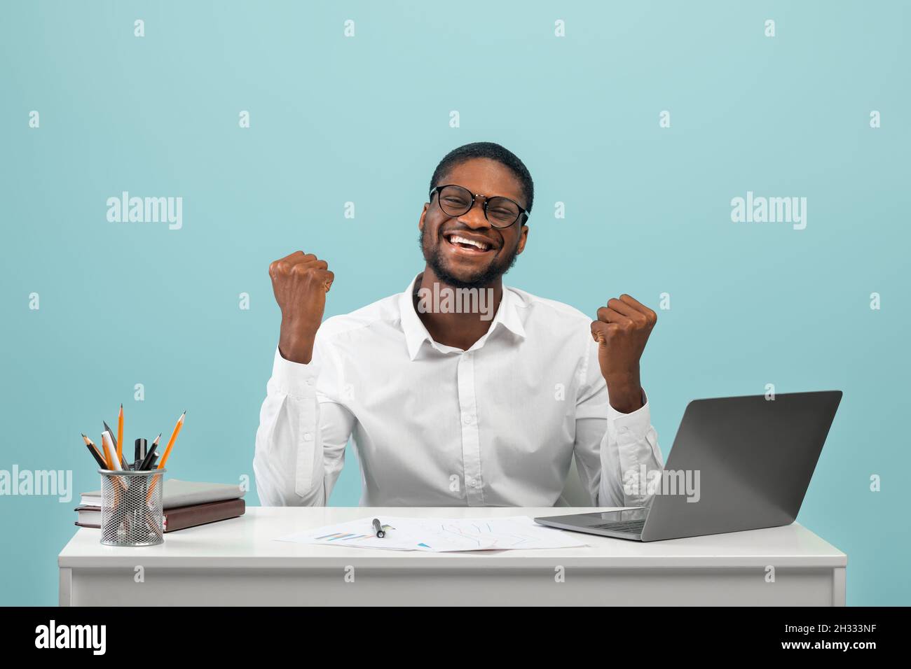 Successful black businessman making YES gesture while working on laptop ...
