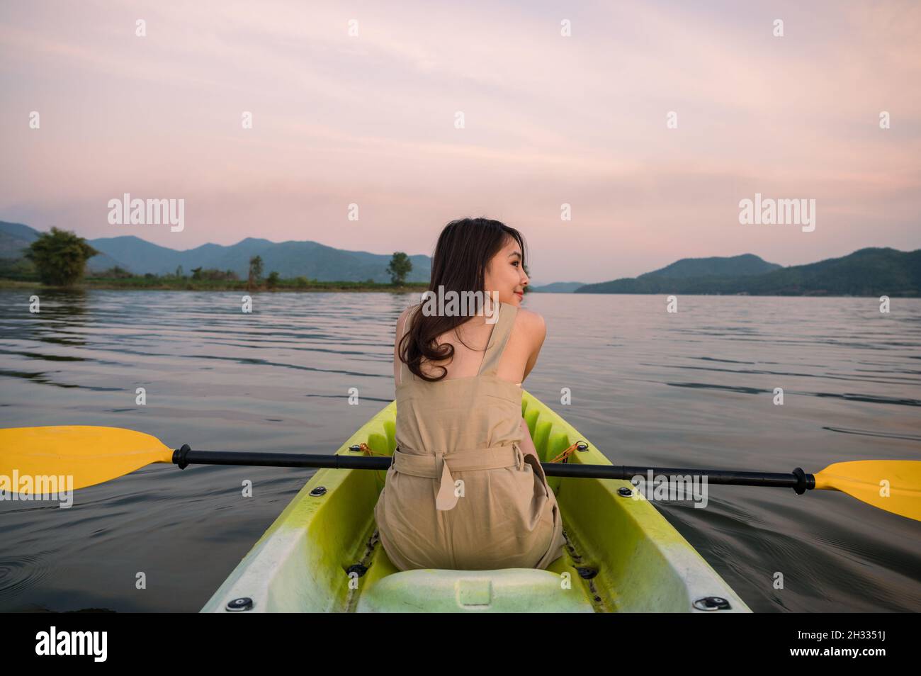 Beautiful young asian woman holding paddle in canoe on lake at evening ...
