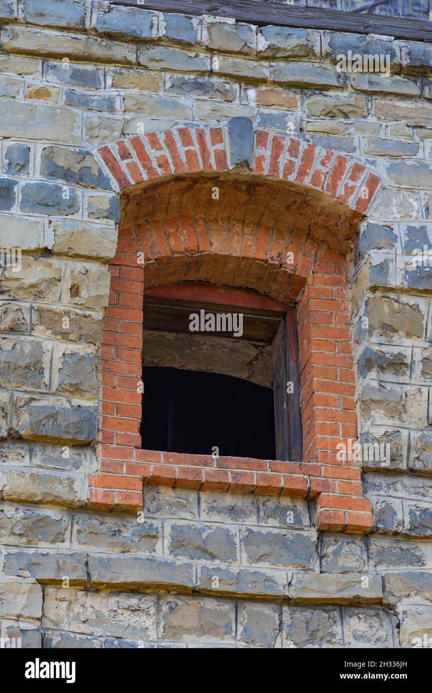 Red brick window of an ancient castle in a wall of natural gray stone ...