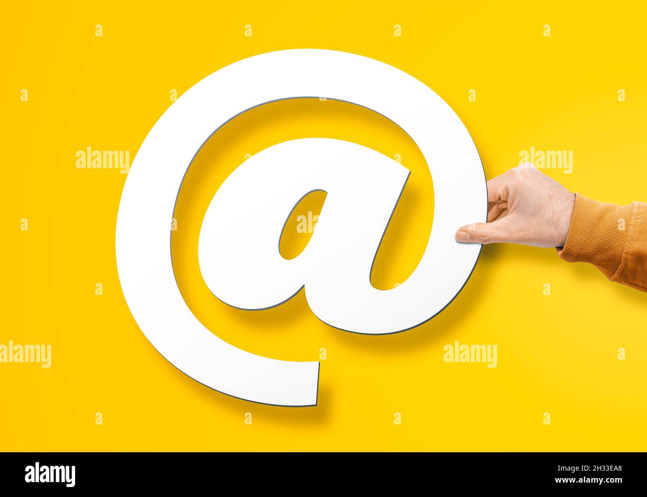 hand holding large at sign against orange background, communication ...