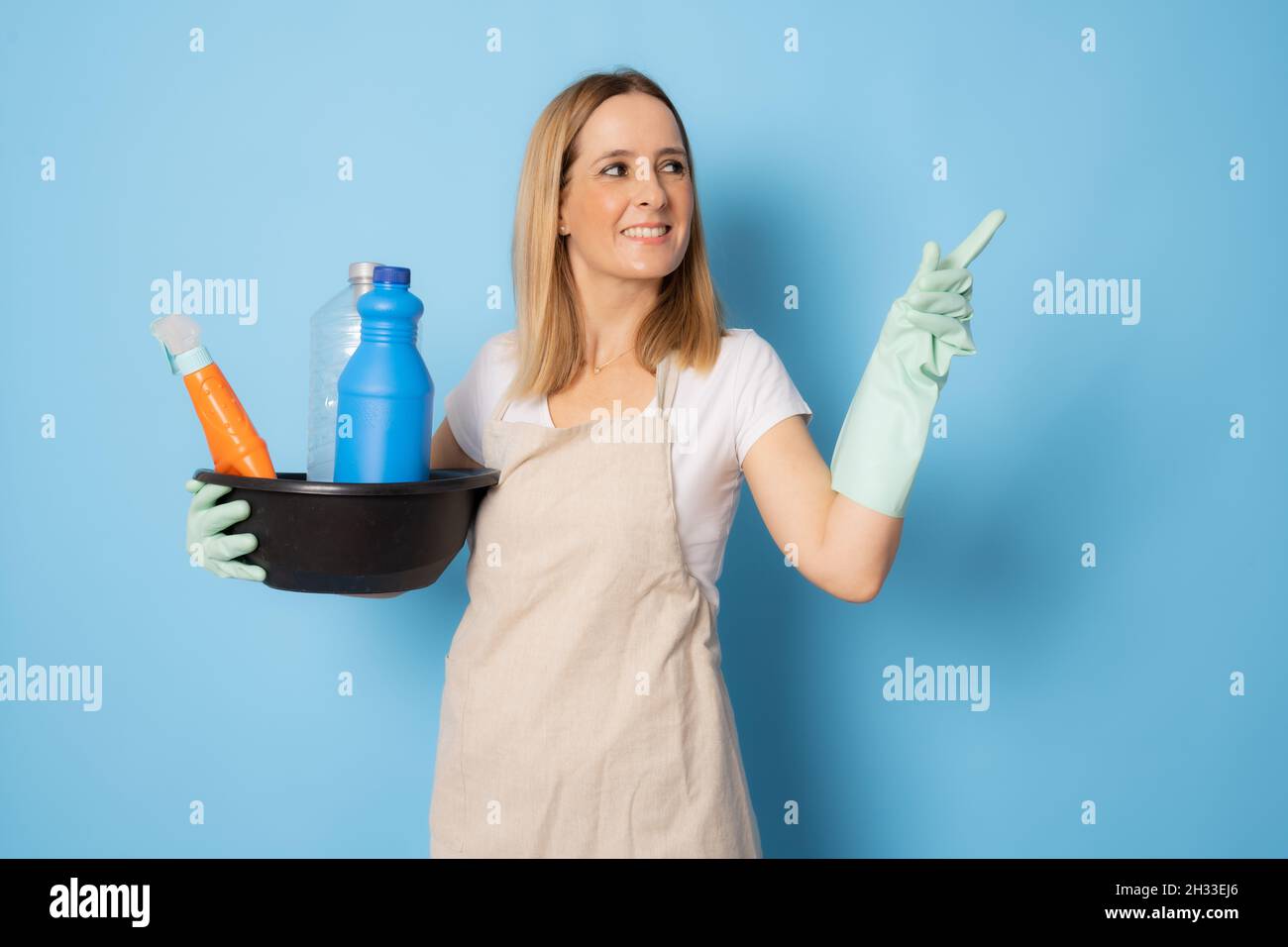 Young smiling cleaner woman pointing finger side. Isolated over blue ...