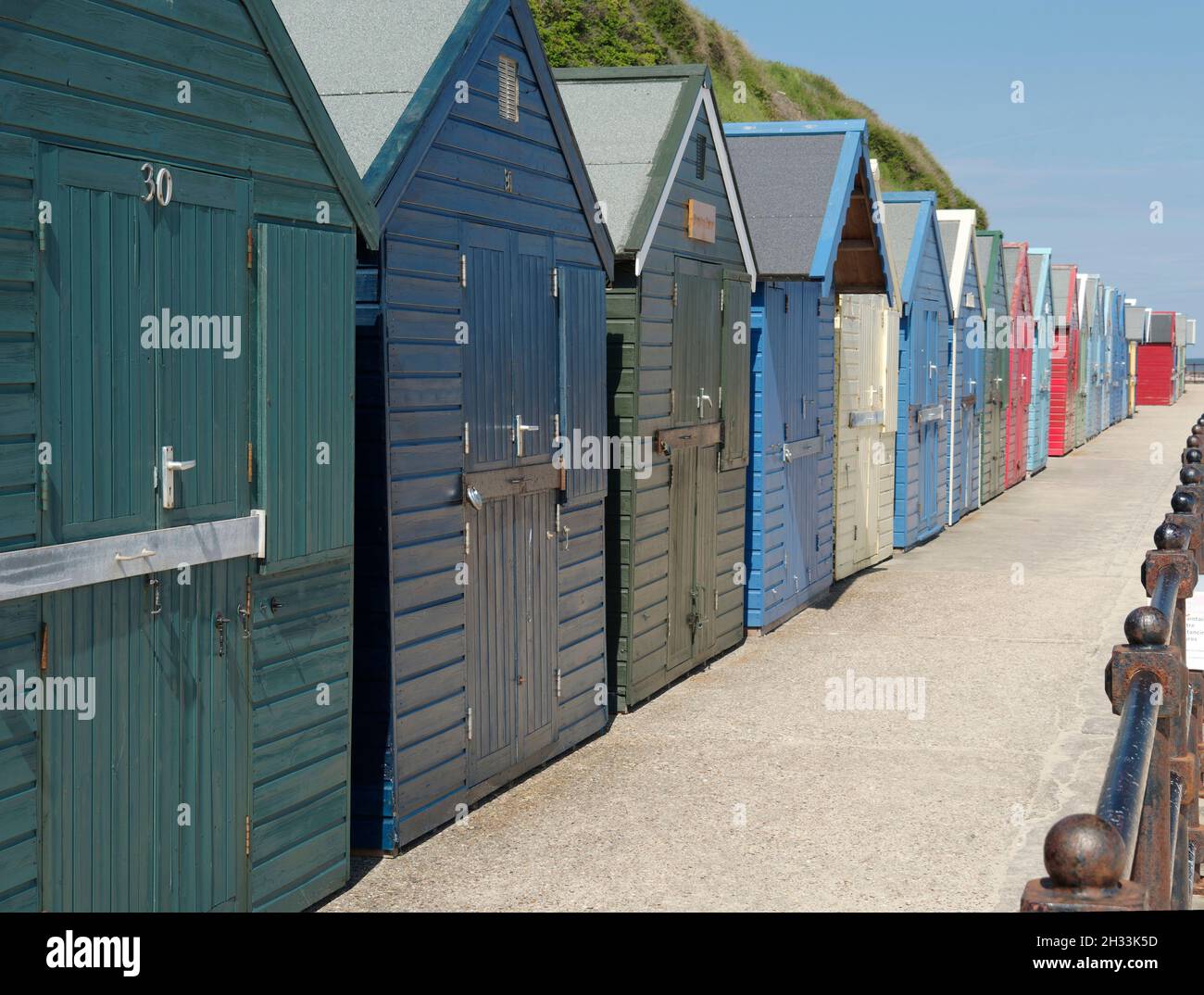 Beach huts line the promenade below the cliffs in the small seaside ...