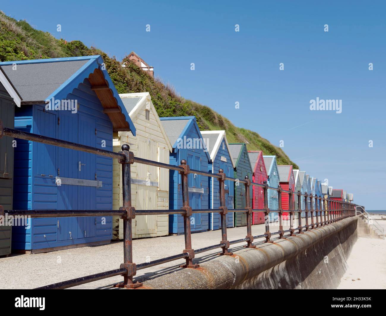 Beach huts line the promenade below the cliffs in the small seaside ...
