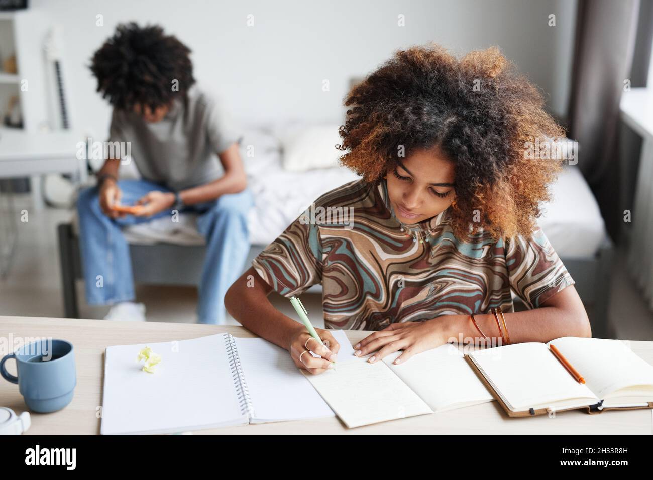 Portrait of female student doing homework and writing in notebook copy ...