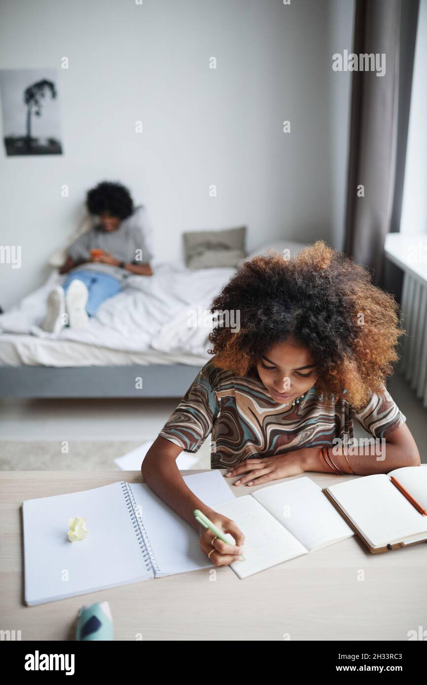 Vertical portrait of female student doing homework and writing in ...