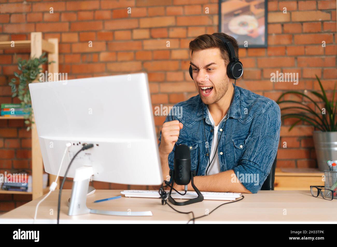 Excited happy audio blogger streamer male wearing headphones sitting at ...