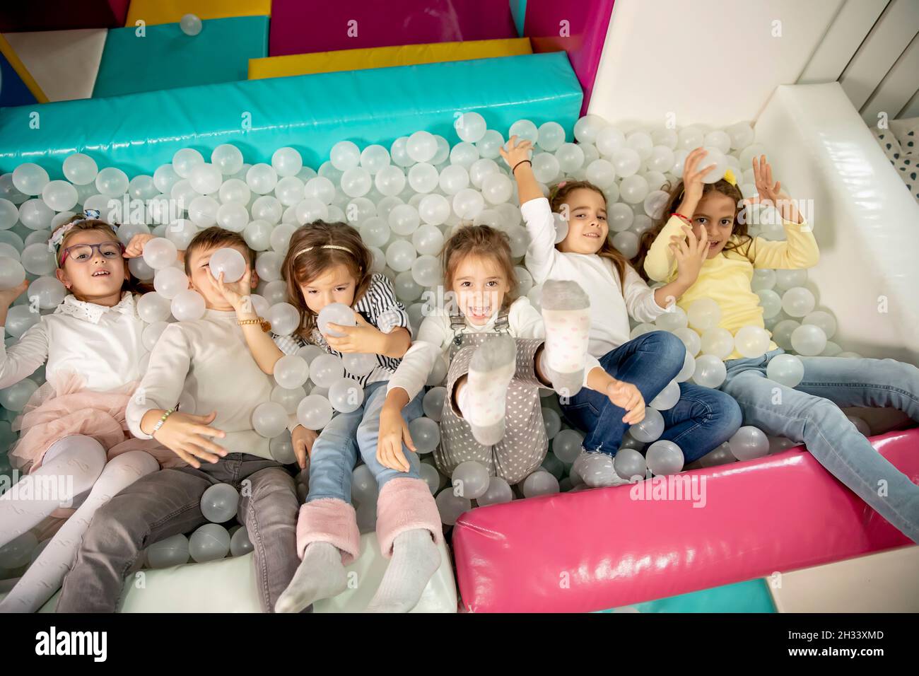 Group of happy little kids in ball pit smiling happily at camera while ...