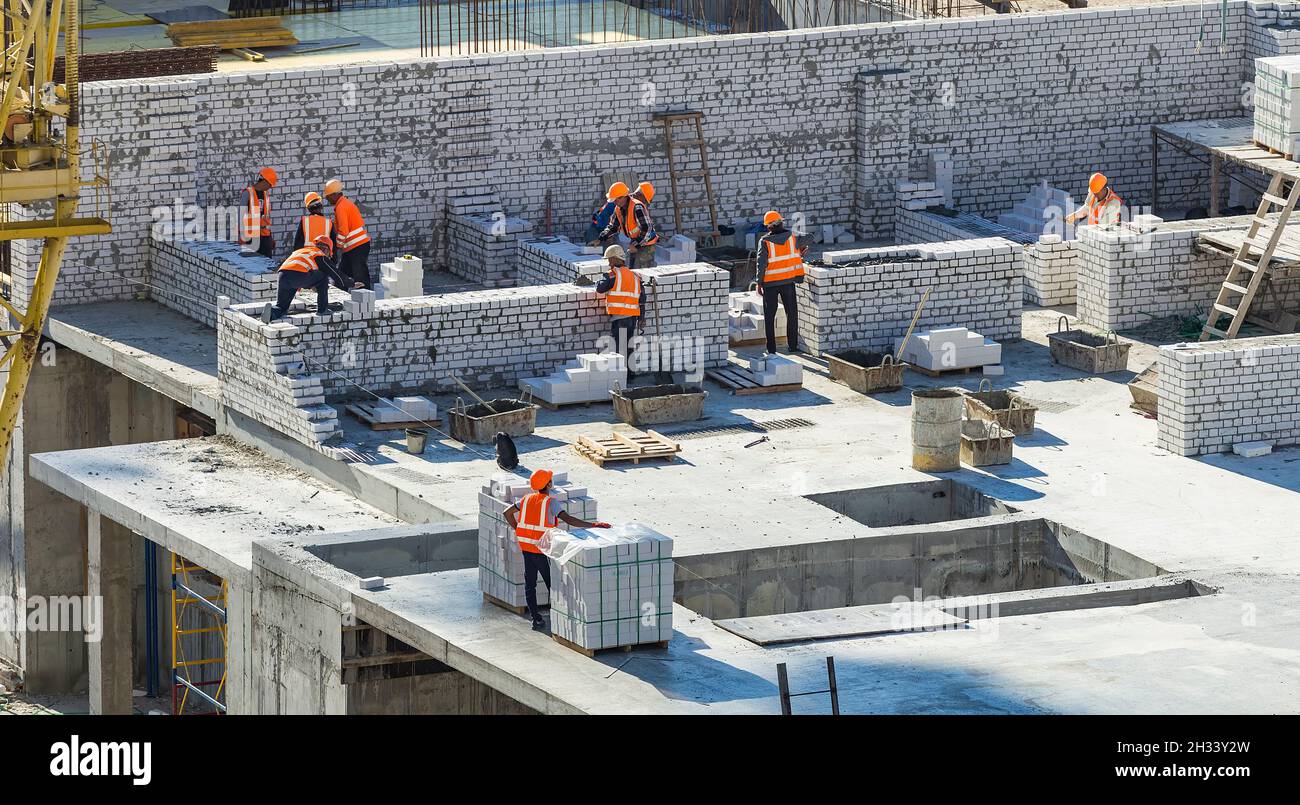 Bricklayer workers in safety orange vests and hard hats make walls of ...