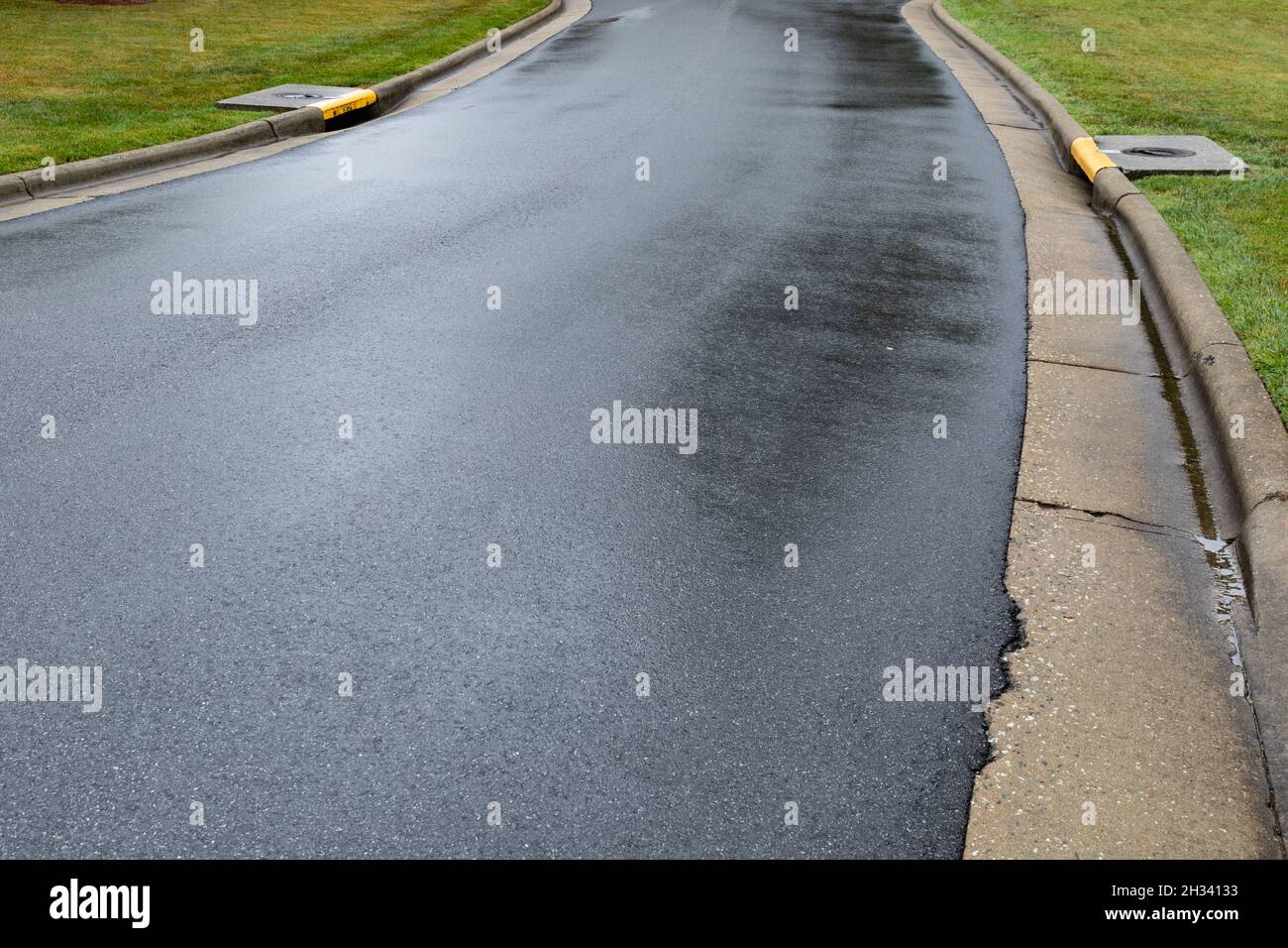 Sweeping asphalt roadway wet from rain, water draining on each side ...