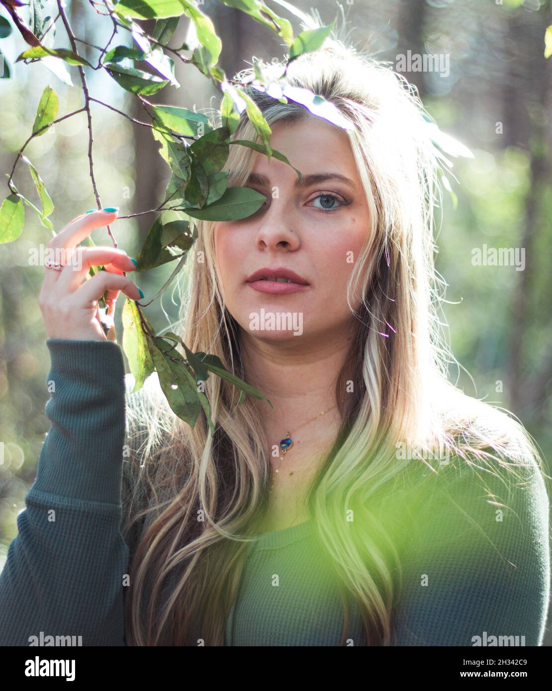 Alluring young woman posing among green leaves gazing at camera with ...