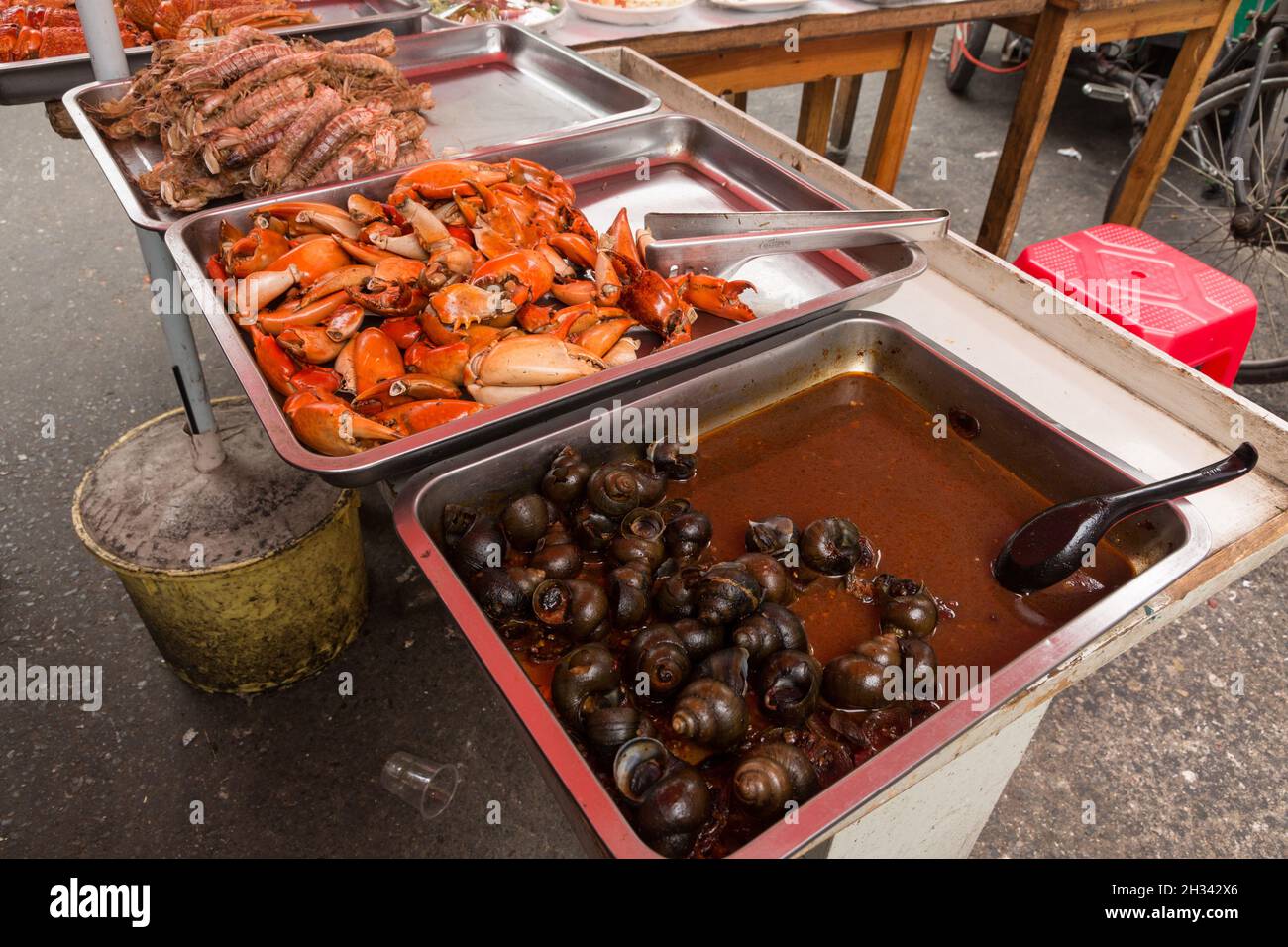 Trays of cooked snails, crab claws and shrimp for sale at an outdoor ...