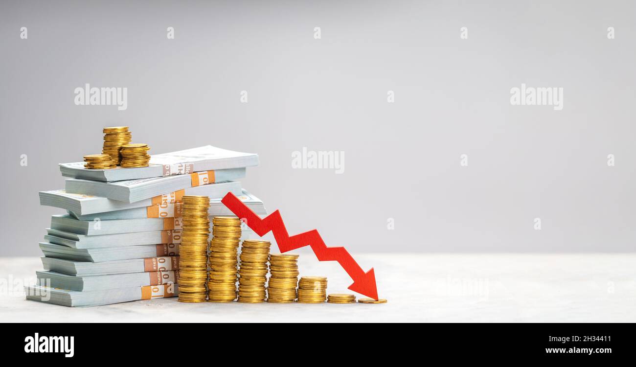 Stack of dollars and gold coins and a red down arrow. The concept of ...