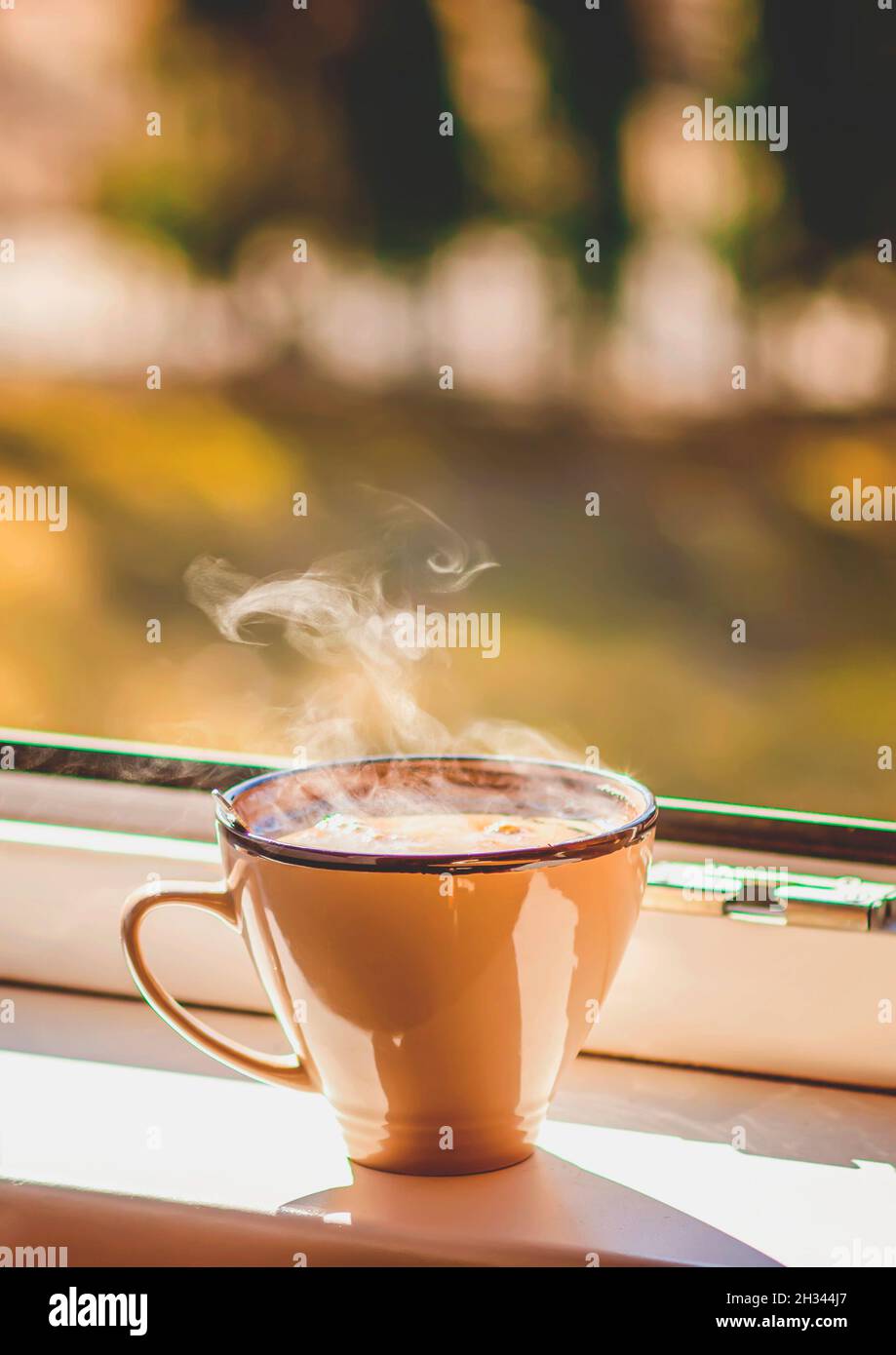 Morning cup of coffee on a window sill. Steam above the ceramics cup ...