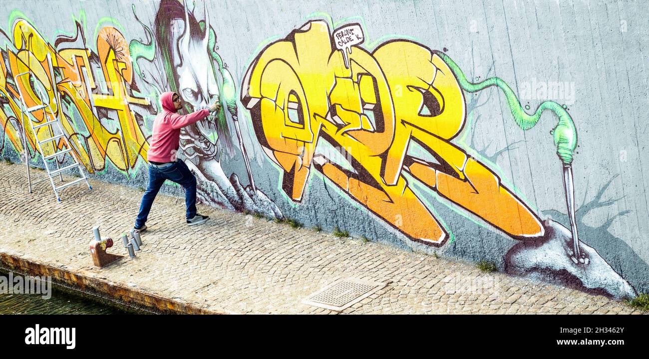 Wide viewof street artist painting colorful graffiti on generic wall ...