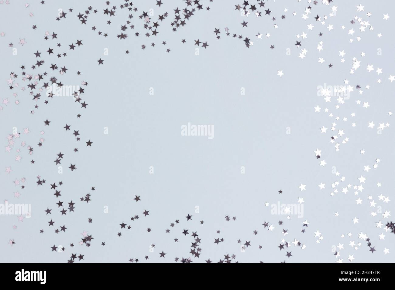 Border frame made of silver colored stars confetti on a blue pastel ...