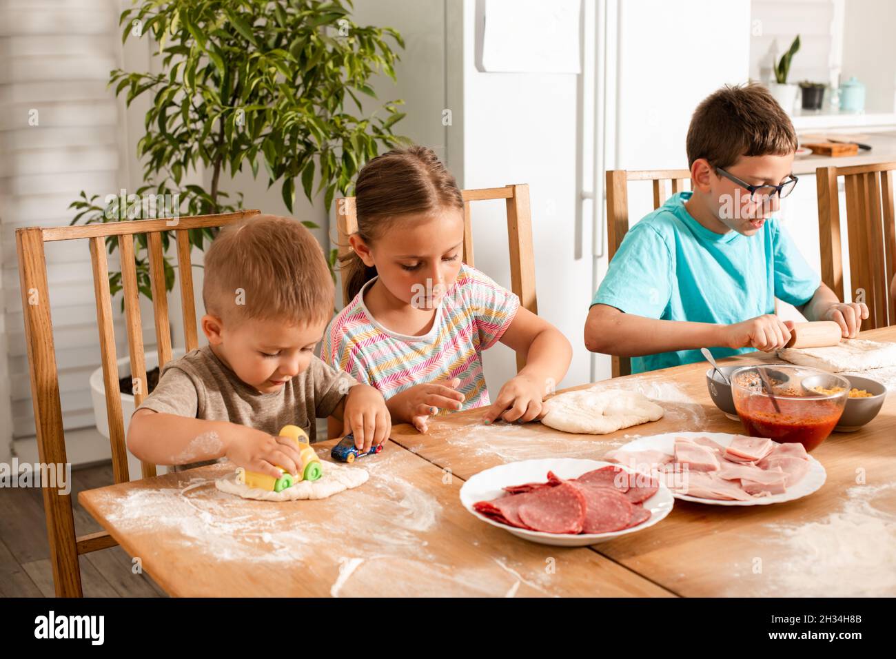 Happy kids sit at a table in the kitchen and make pizza Stock Photo - Alamy
