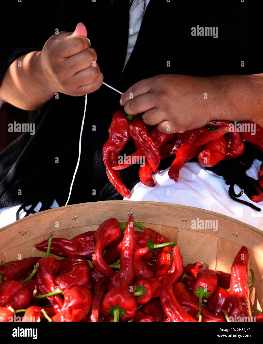 A woman demonstrates how to make traditional ristras by stringing red ...