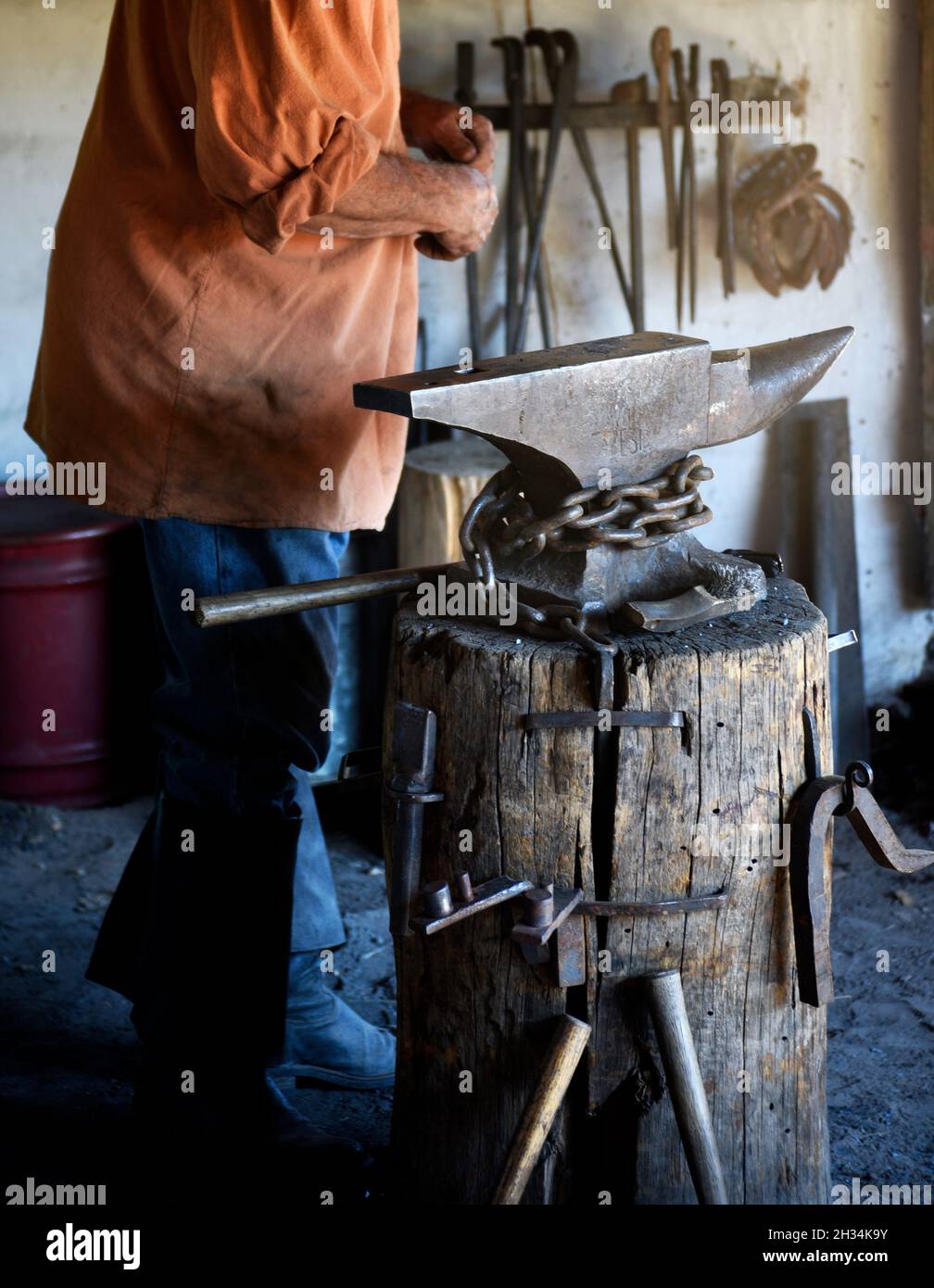 A blacksmith works with an iron and an anvil in the blacksmith shop at ...
