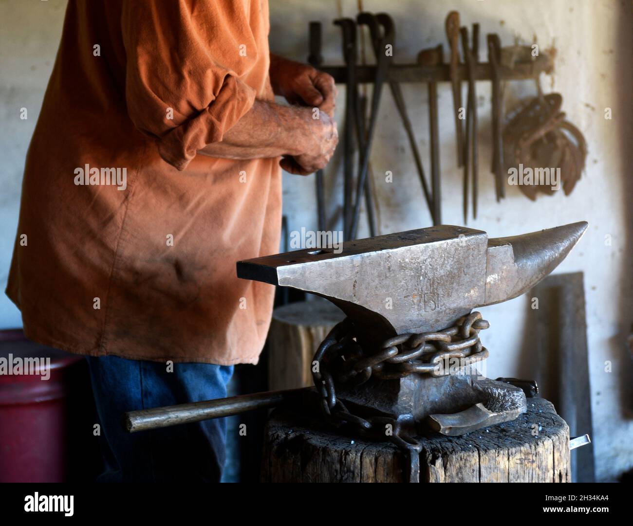 A blacksmith works with an iron and an anvil in the blacksmith shop at ...